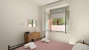 Quarto com cama, cómoda de madeira, espelho e janela com vista para o verde lá fora.