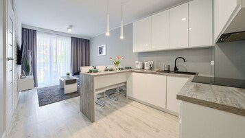 Cozinha moderna com armários brancos, bancada de mármore e área de jantar com mesa e cadeiras.