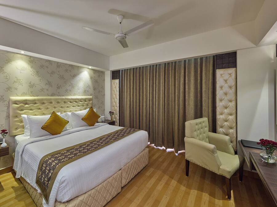 Quarto de hotel com uma cama grande, uma cadeira, uma escrivaninha e um ventilador de teto.