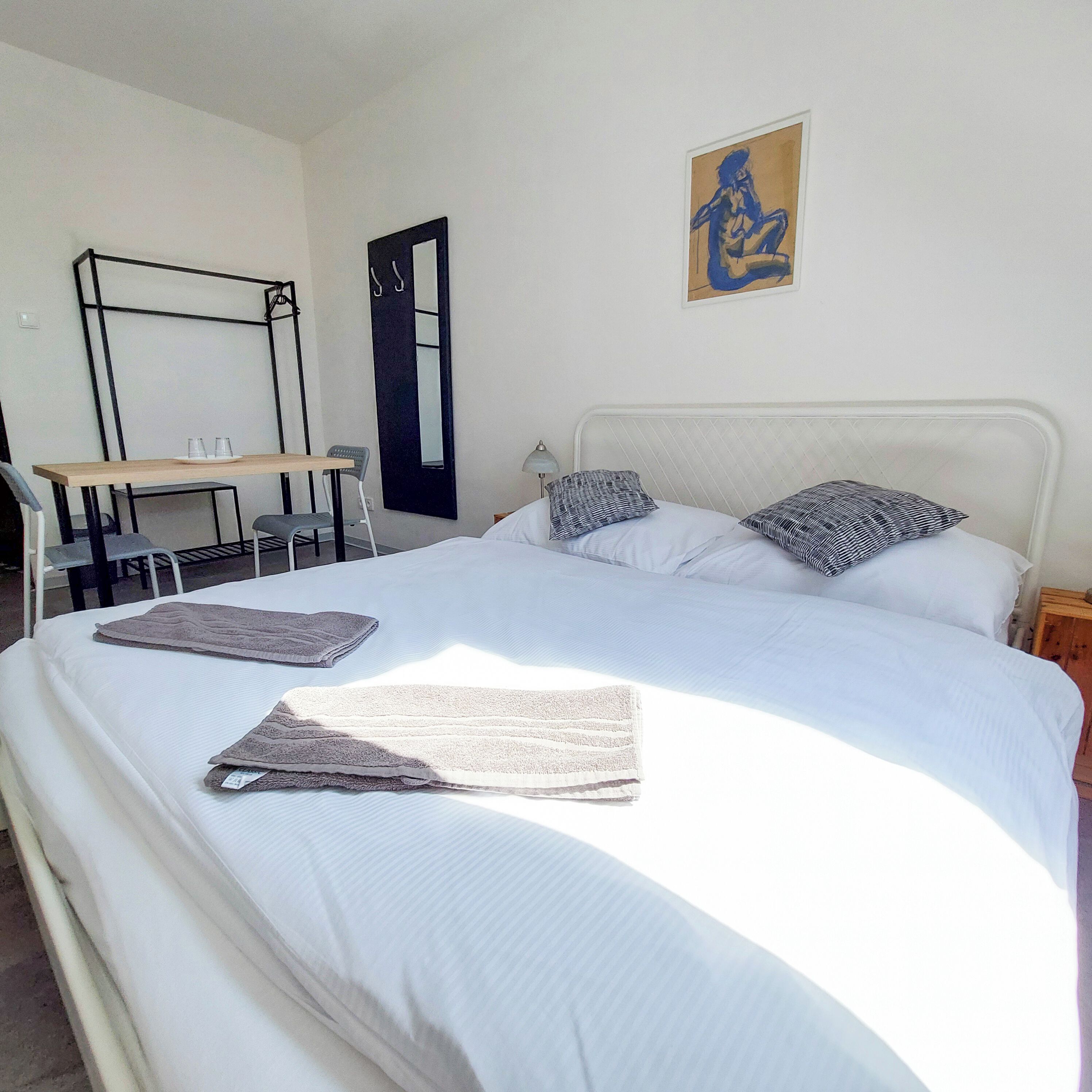 Quarto com cama grande, duas almofadas, mesa de cabeceira, cadeira, escrivaninha e espelho.