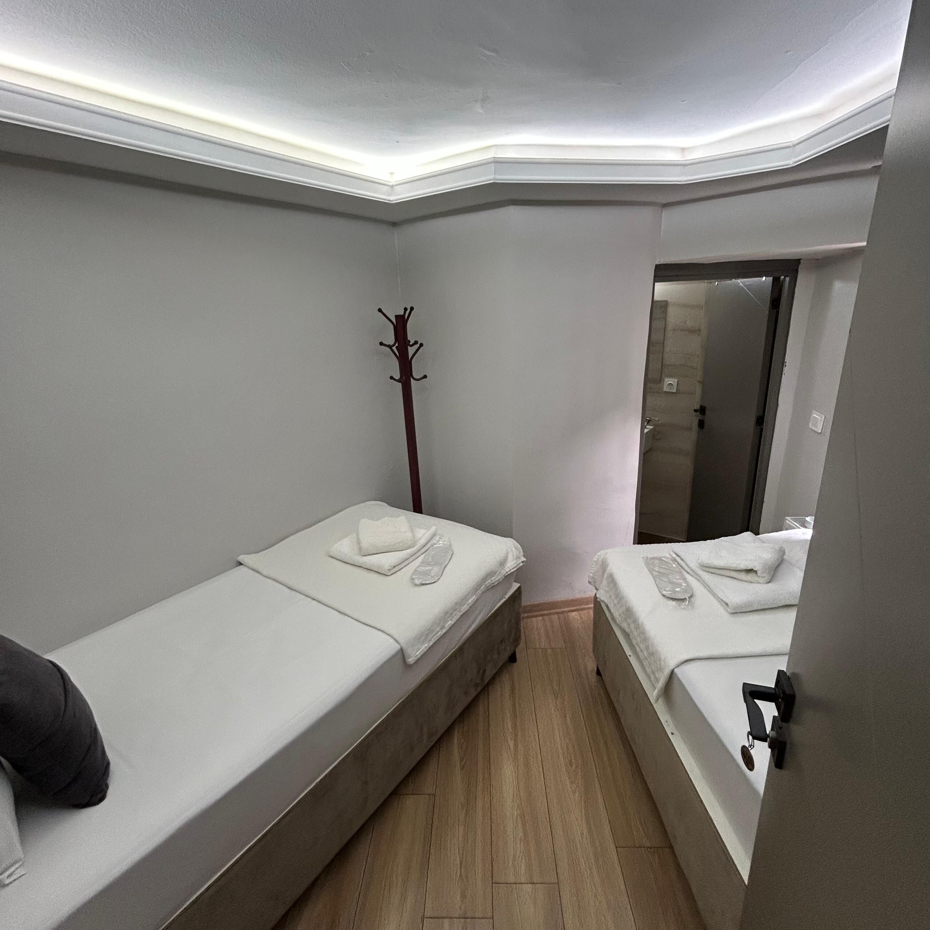Quarto pequeno e moderno com duas camas individuais, um cabideiro e um espelho.