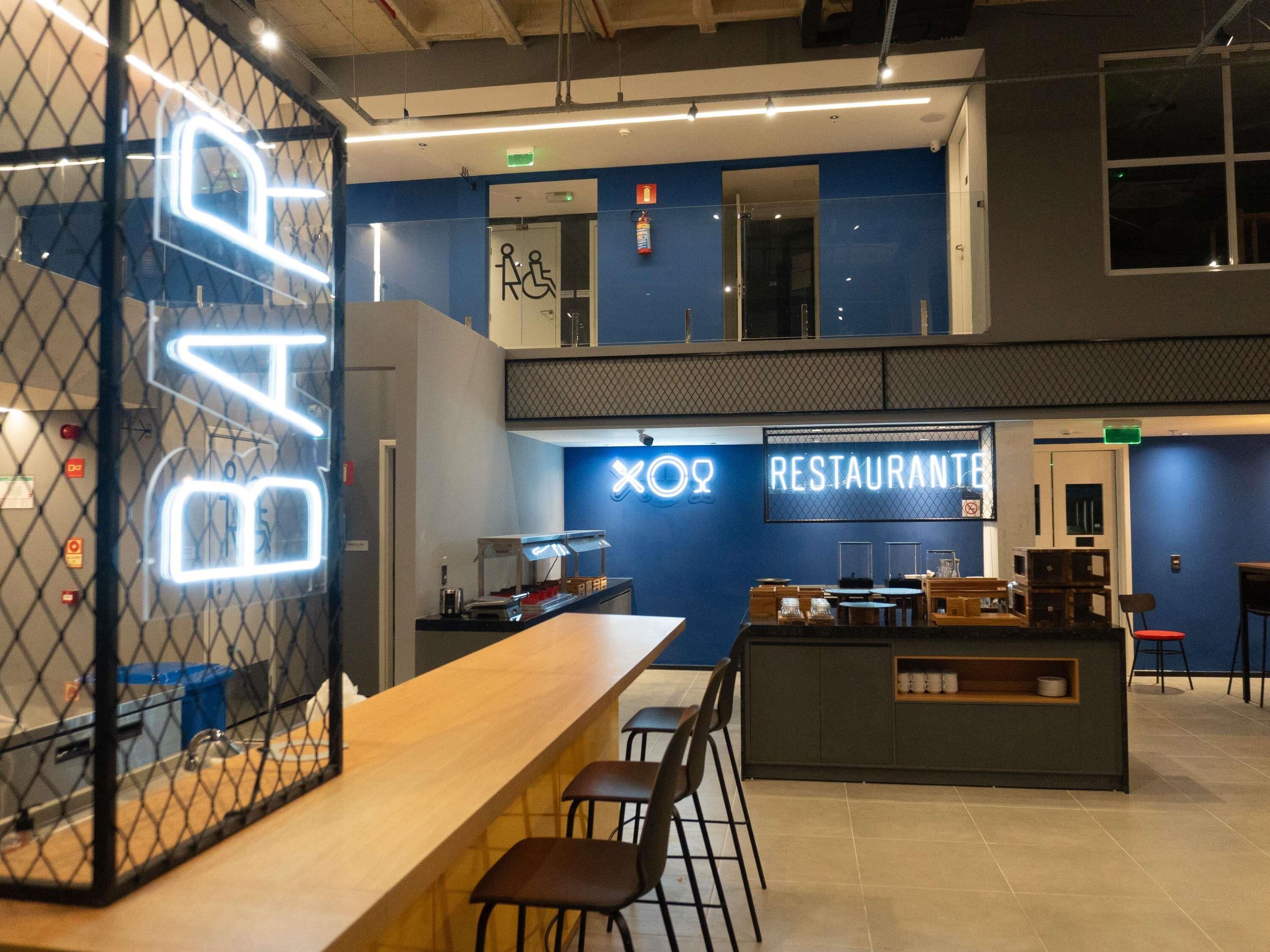 Uma área de bar moderna com um letreiro de neon, um balcão e assentos.