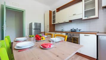 Uma cozinha moderna com armários brancos, bancada de madeira e mesa de jantar posta com pratos, talheres e frutas.