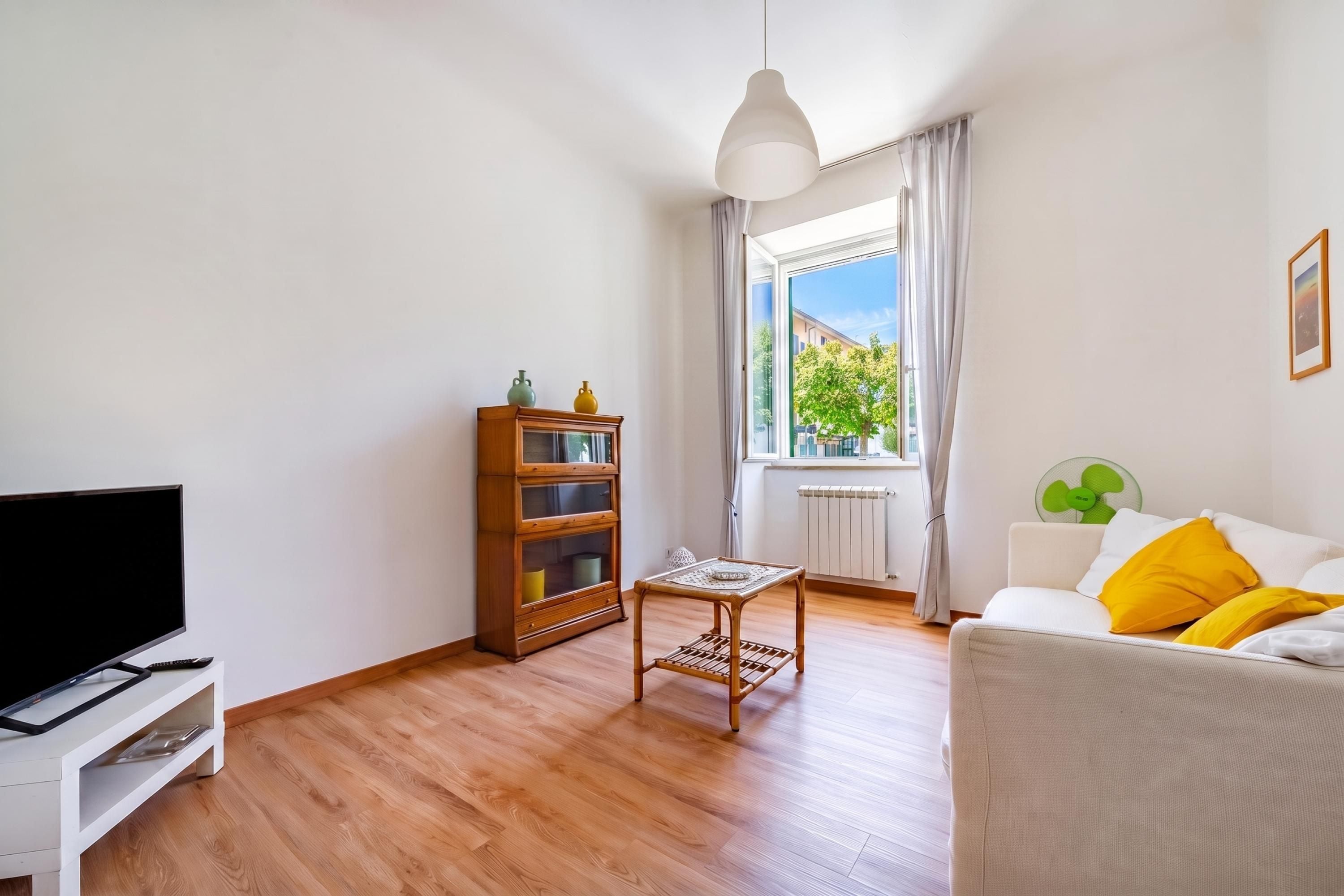 Uma sala de estar com televisão de tela plana, móveis de madeira, uma janela com cortinas e um ventilador verde.