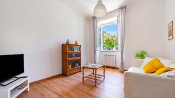 Uma sala de estar com televisão de tela plana, móveis de madeira, uma janela com cortinas e um ventilador verde.