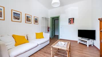 Uma sala de estar com um sofá branco, uma televisão e quadros nas paredes.