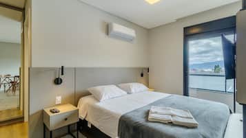 Quarto de hotel moderno com uma cama grande, mesa de cabeceira e vista da cidade através de uma janela ampla.