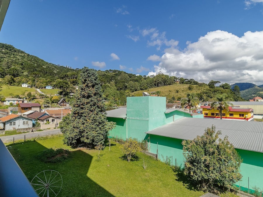 Bairro residencial com casas, um edifício verde e uma colina ao fundo.