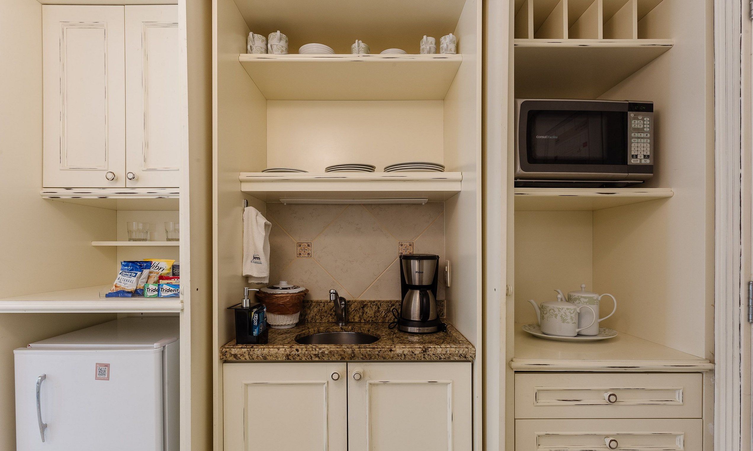 Cozinha compacta equipada com micro-ondas, cafeteira e chá.