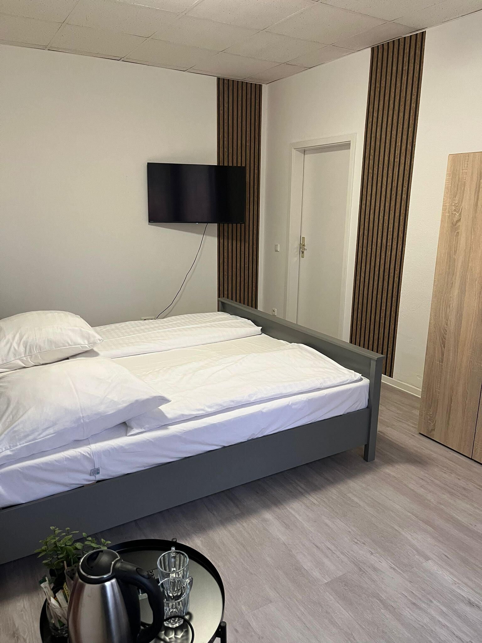Um quarto moderno com cama, televisão de tela plana na parede e guarda-roupa de madeira.