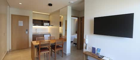 Quarto de hotel moderno com área de jantar, televisão de tela plana na parede e uma pequena estante com folhetos informativos.