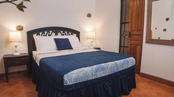 Quarto com cama, duas mesas de cabeceira com luminárias, porta de madeira e espelho fixado na parede.
