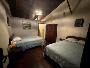 Quarto com duas camas, um guarda-roupa de madeira, um quadro na parede e um lustre.