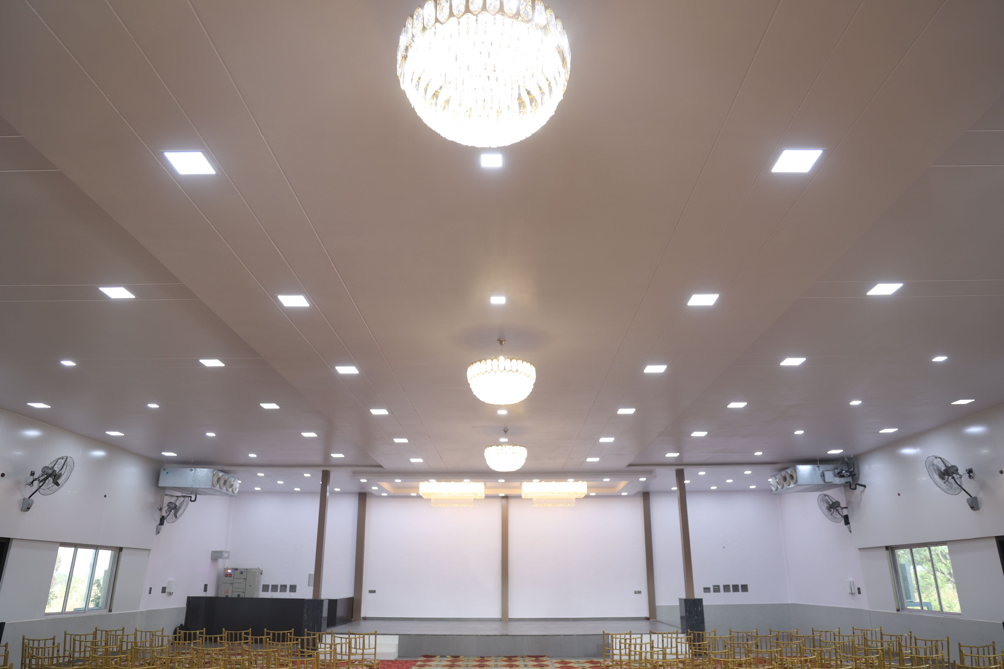 Um salão amplo e bem iluminado, com um lustre, ventiladores de teto e fileiras de cadeiras.