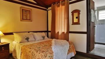 Quarto com cama, mesa de cabeceira, espelho e porta para uma varanda.