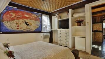 Quarto com cama, televisão, penteadeira e um quadro na parede.