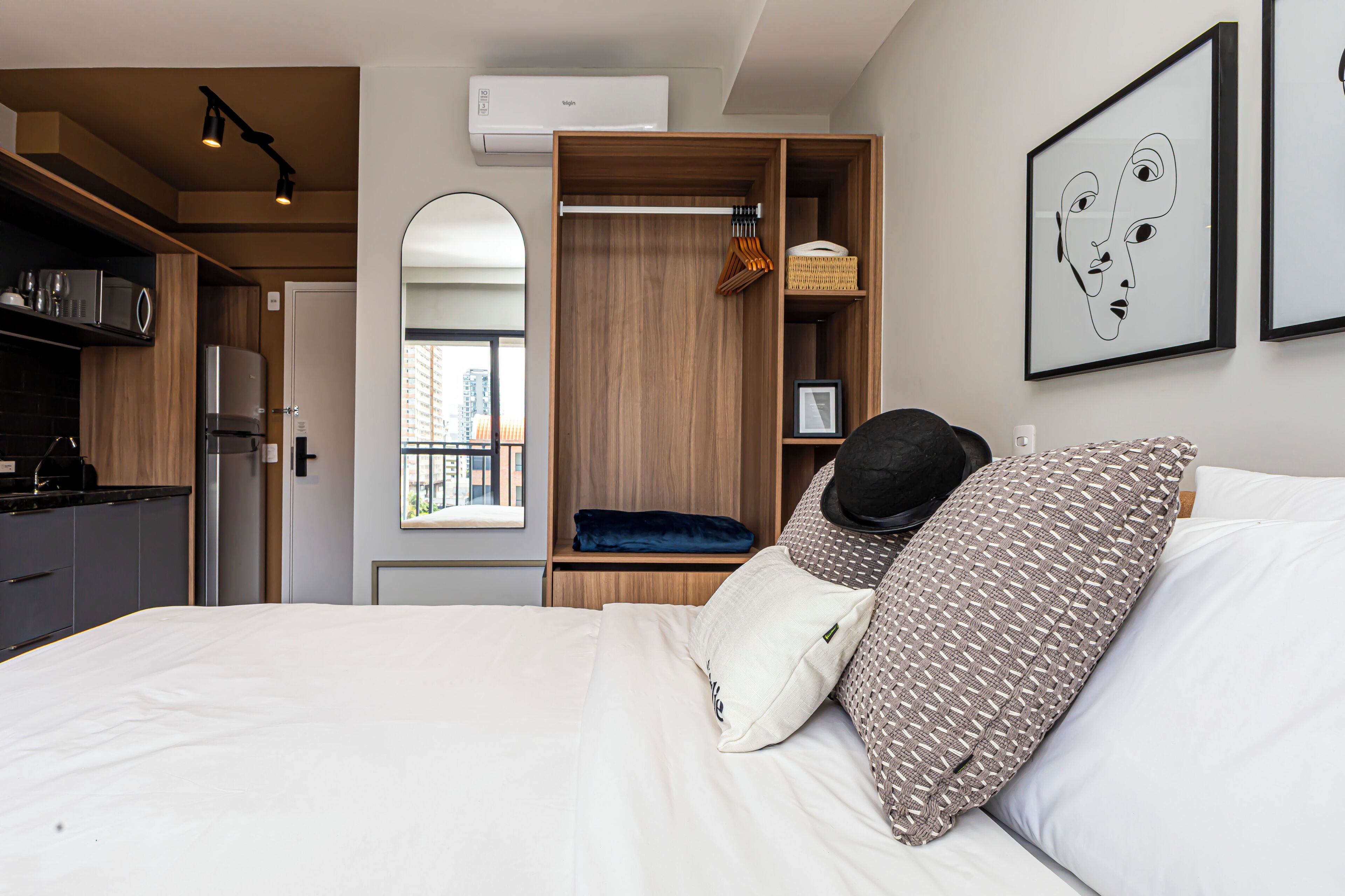 Quarto com cama, guarda-roupa, espelho e uma kitchenette.