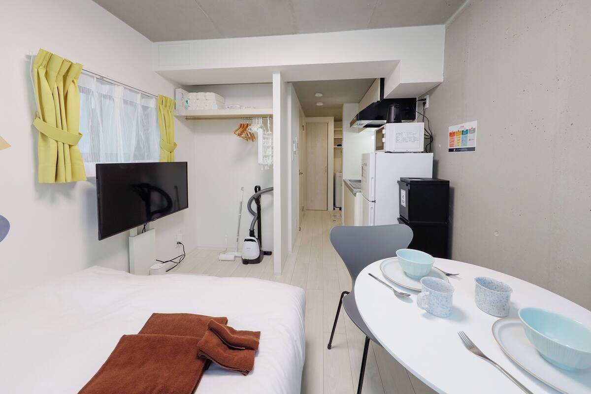 Quarto de hotel com cama, televisão, escrivaninha com cadeira, micro-ondas e frigorífico.