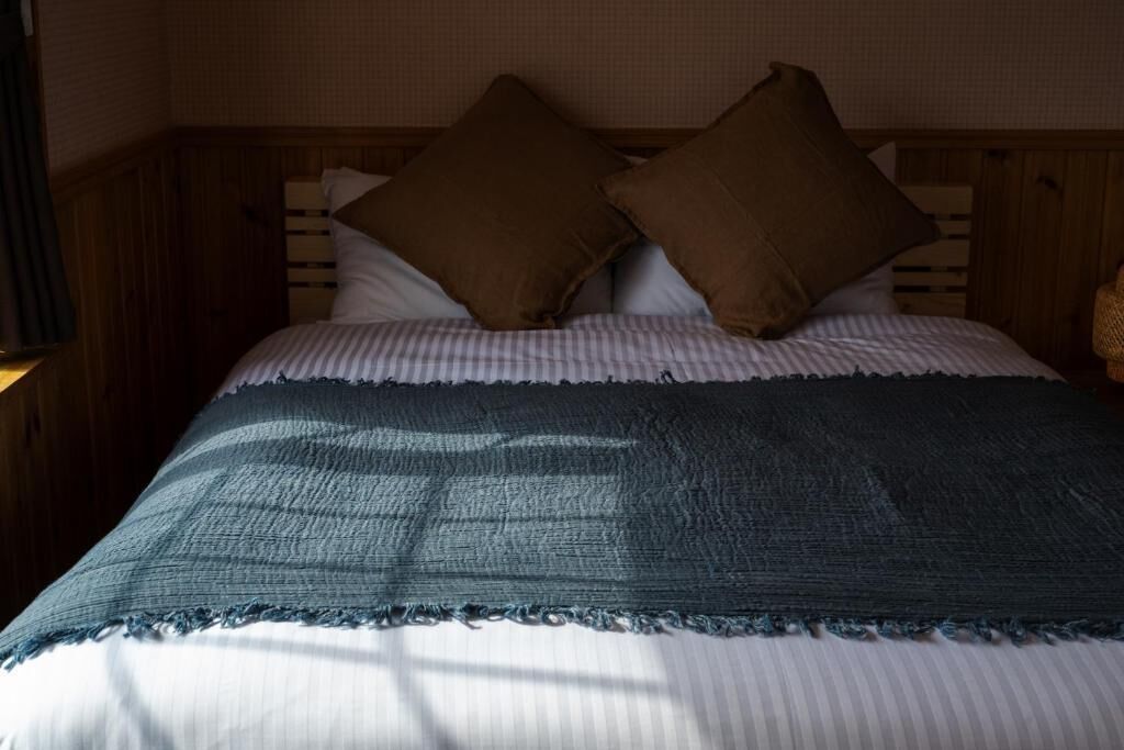 Cama com roupa de cama listrada e duas almofadas, um cobertor azul escuro e cabeceira de madeira.