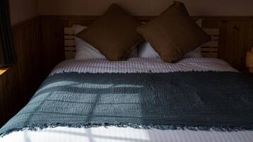 Cama com roupa de cama listrada e duas almofadas, um cobertor azul escuro e cabeceira de madeira.