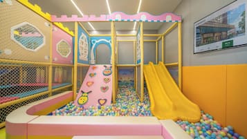 Espaço de recreação infantil com escorregador, piscina de bolinhas e estruturas de jogo com redes.