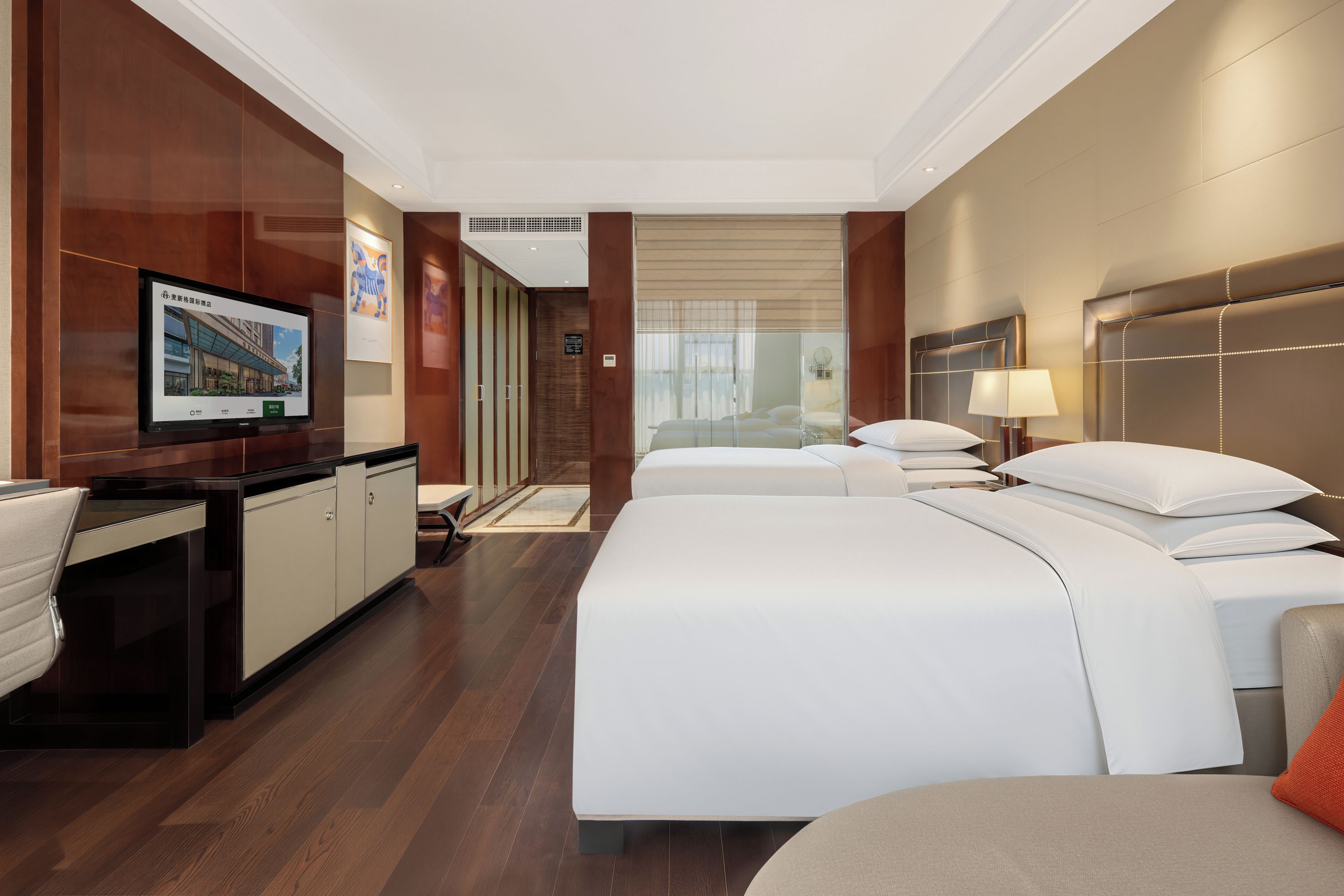 Quarto de hotel com uma cama grande, uma escrivaninha com computador, televisão e banheiro visível através de uma porta de vidro.
