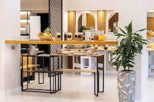 Um balcão de café da manhã moderno com diversas opções de alimentos, uma máquina de café e uma planta decorativa.