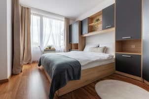 Quarto moderno com cama de madeira, armários embutidos escuros e janela com cortinas leves.