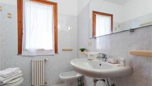 Casa de banho com uma pia branca, sanita, bidé, porta-toalhas e janela com cortinas.