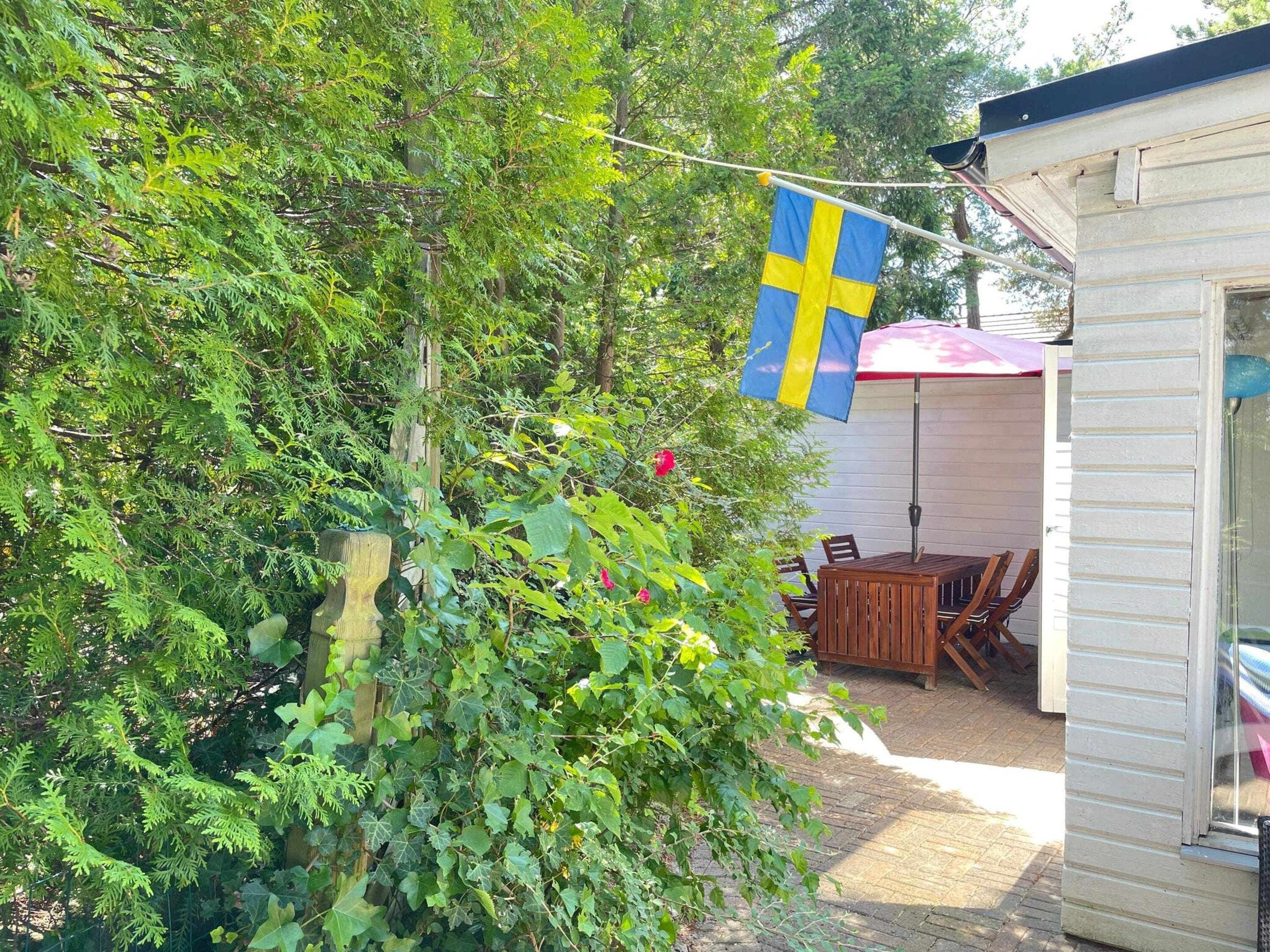 Um jardim com uma bandeira sueca, uma mesa de madeira e cadeiras.