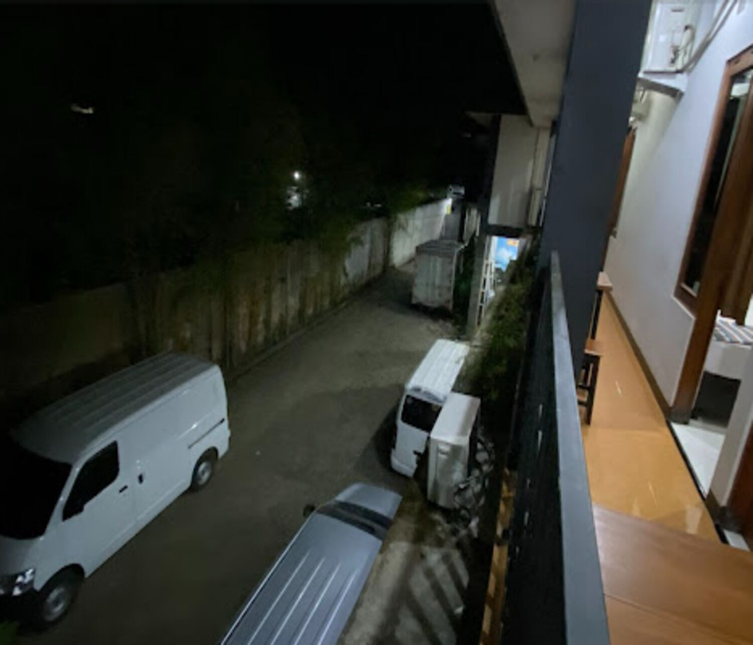 Uma área de estacionamento com duas carrinhas brancas, uma estrutura de metal e um edifício com varanda.