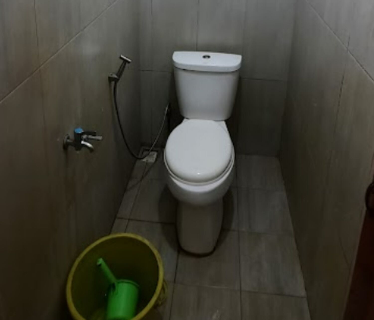 Uma casa de banho pequena com um chuveiro, uma sanita e um balde verde.