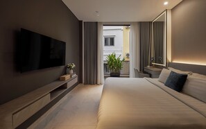 Quarto de hotel moderno com uma cama grande, televisão de tela plana, mesa de cabeceira e um vaso de planta.