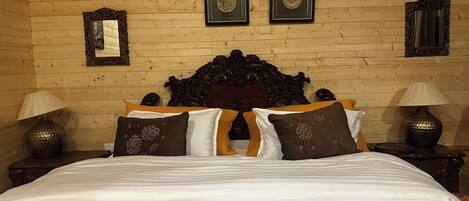 Quarto com painéis de madeira, uma cama grande, duas fotos emolduradas na parede e duas luminárias de cada lado da cama.