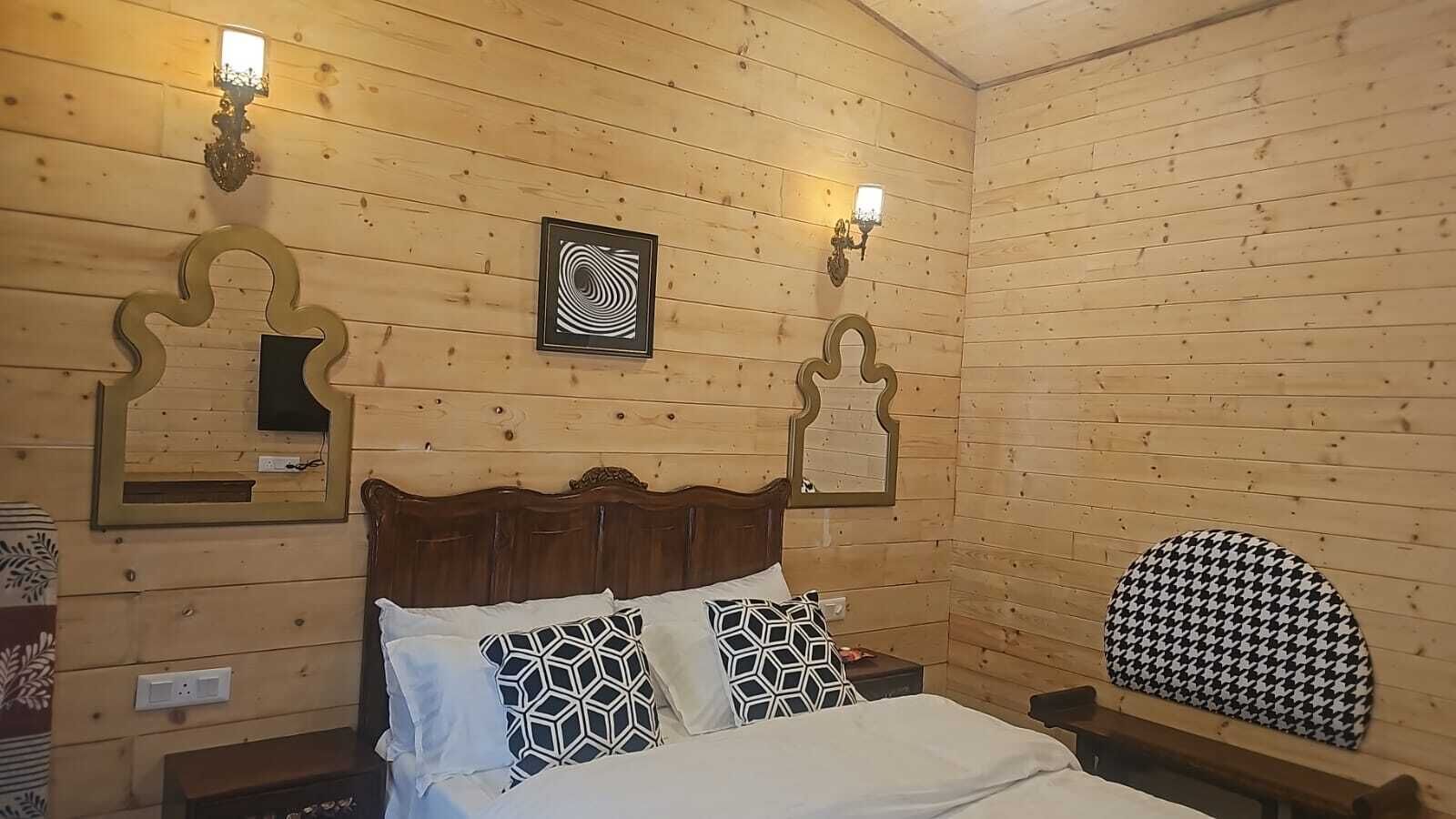 Quarto com painéis de madeira, uma cama, duas arandelas e um espelho decorativo.