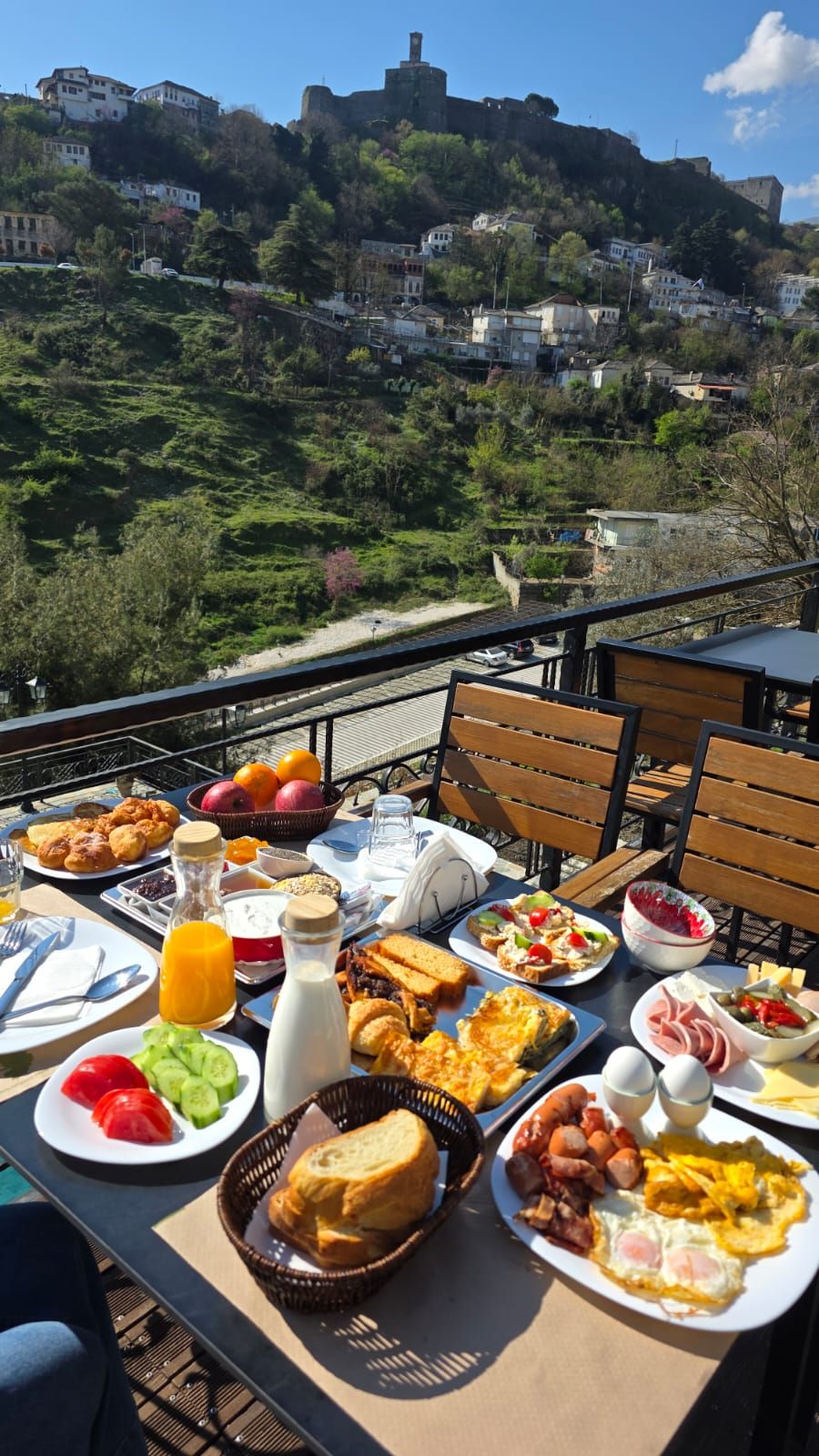 Mesa posta com alimentos para o café da manhã e vista panorâmica de uma cidade no morro.