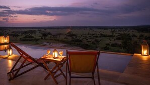 Vista do pôr do sol a partir de uma área externa com mesa e cadeiras, com vista para a paisagem.