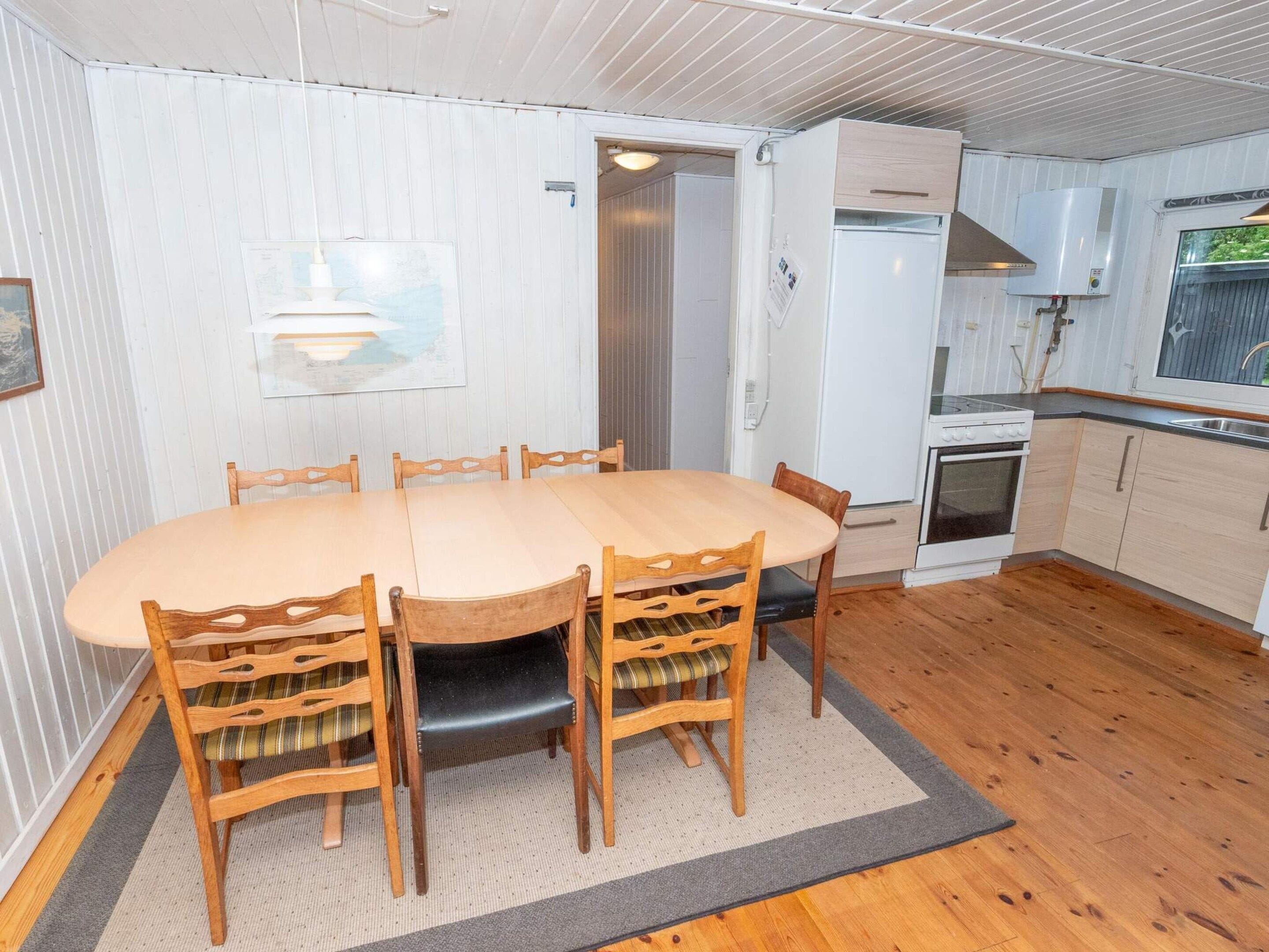 Cozinha compacta com área de refeições, apresentando uma mesa redonda e cadeiras de madeira, forno embutido e janela com vista para vegetação.