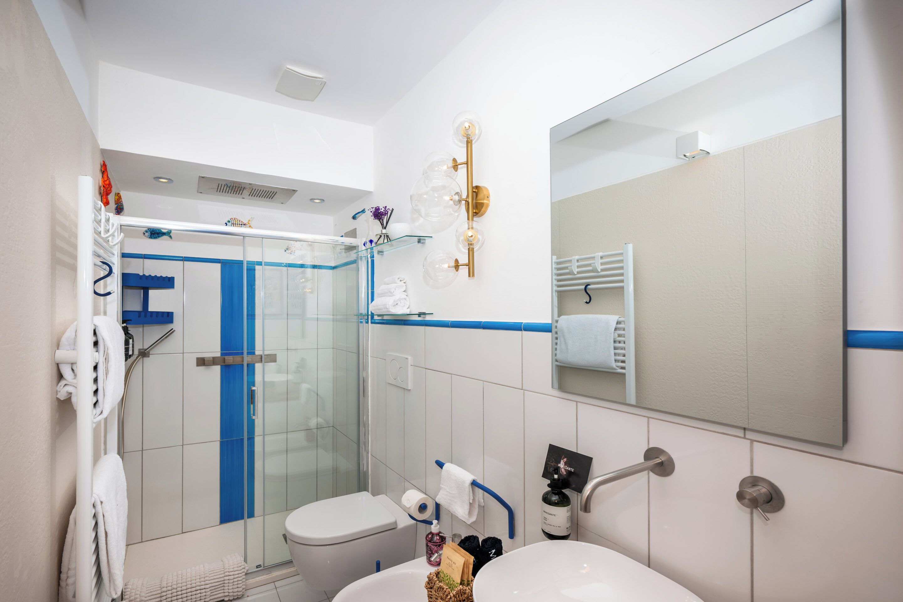 Um banheiro moderno com box de vidro, vaso sanitário branco, pia com espelho e porta-toalhas.