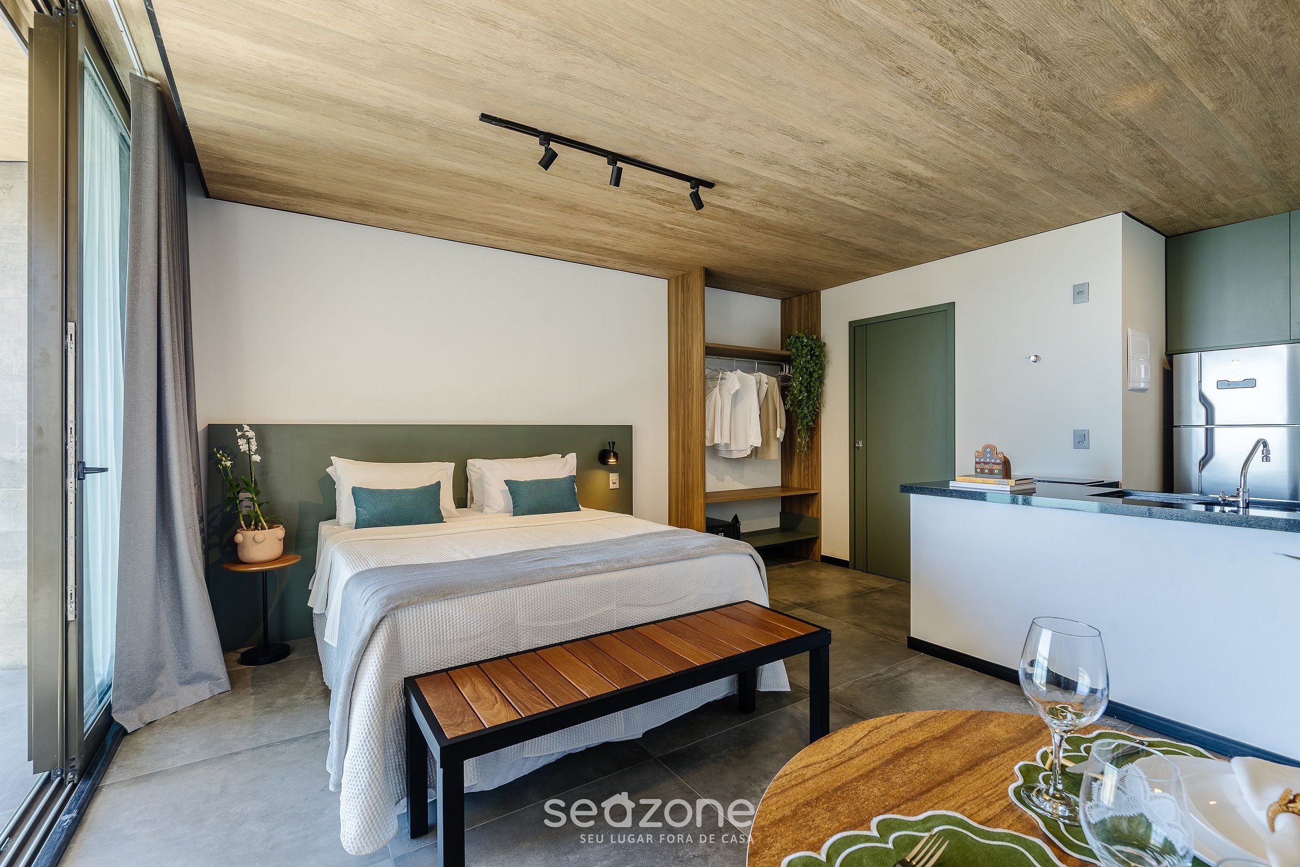 Quarto moderno com cama, mesa de cabeceira, banqueta e um copo de vinho sobre uma mesa.