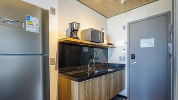 Cozinha compacta com geladeira de aço inoxidável, micro-ondas e máquina de café sobre a bancada.