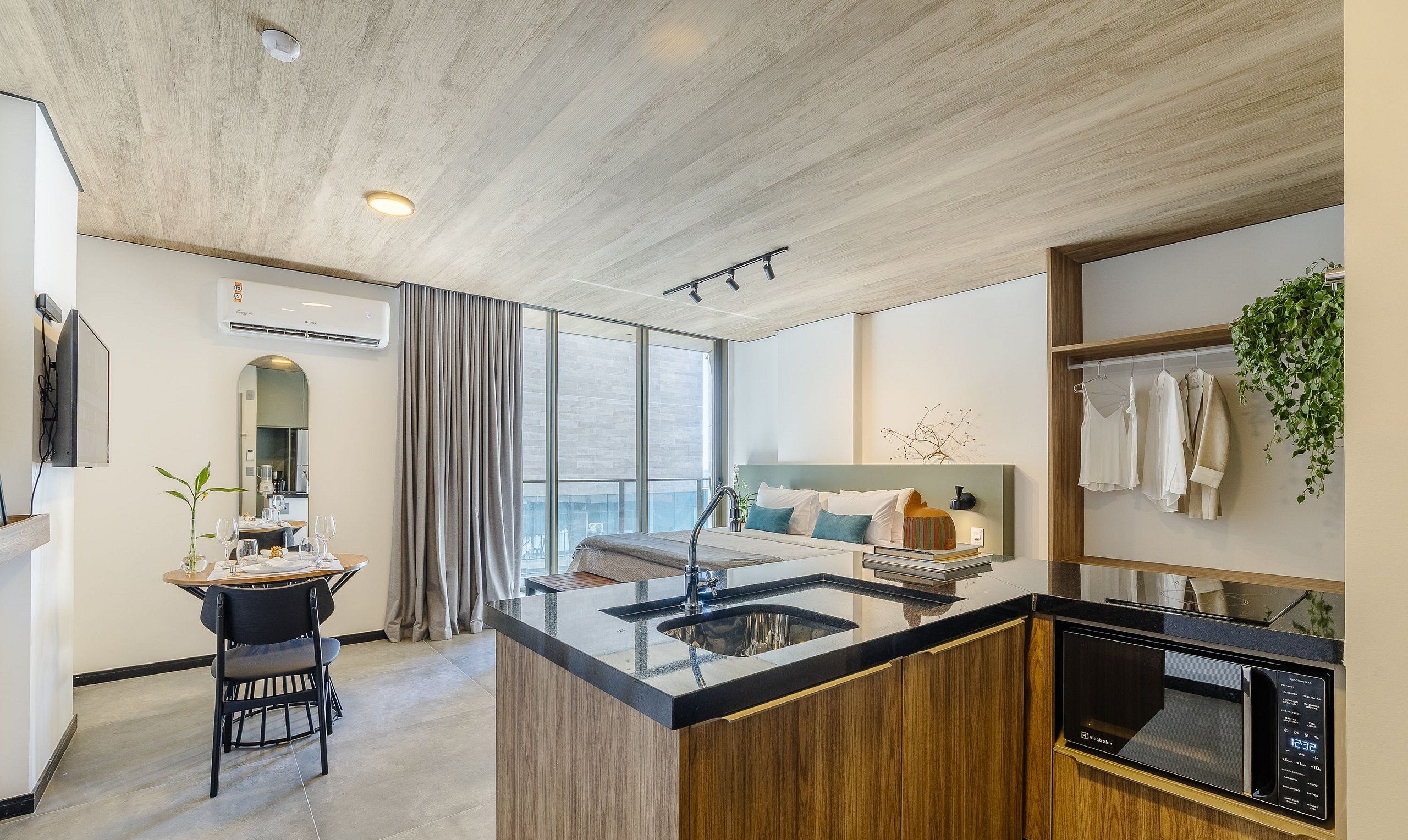 Quarto de hotel moderno com cozinha, mesa de jantar e uma janela grande.