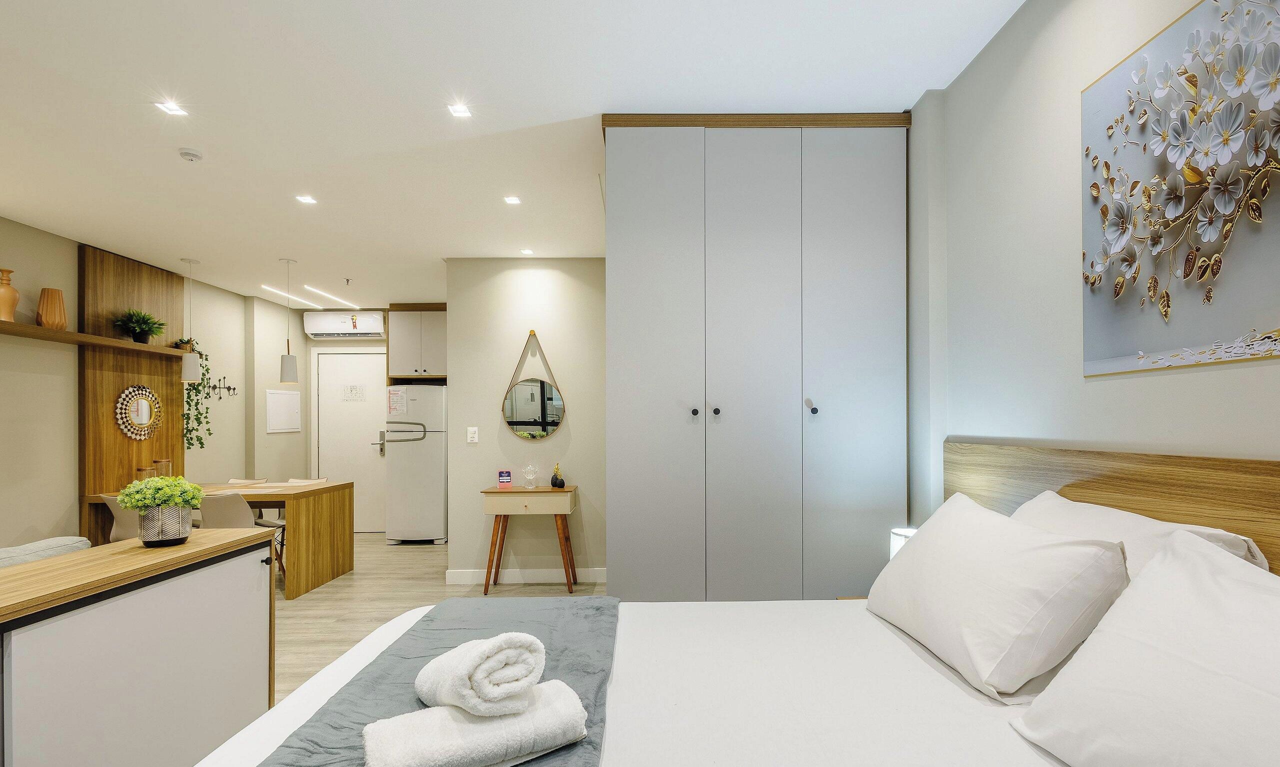 Quarto de hotel moderno com uma cama, uma escrivaninha, uma cadeira, um espelho e um guarda-roupa.
