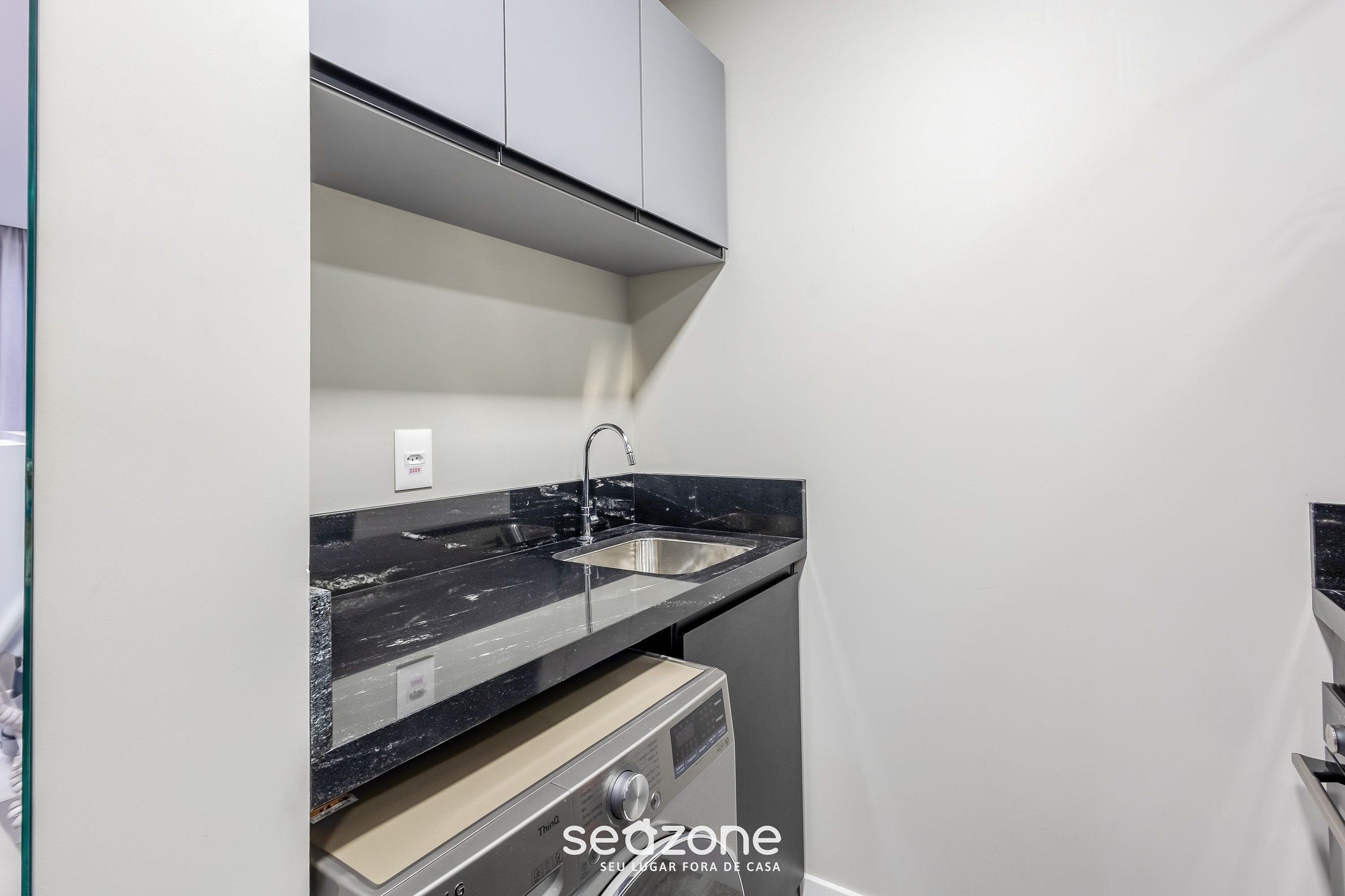 Uma cozinha compacta com bancada de mármore preto, pia de aço inoxidável e lava-louças embutida.