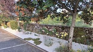 Um parque de estacionamento ao lado de uma parede de pedra, com diversos canteiros de plantas e flores.