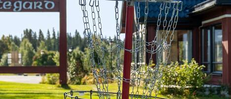 Cesto de disc golf com cerca de arame, um mastro vermelho e uma placa de metal.