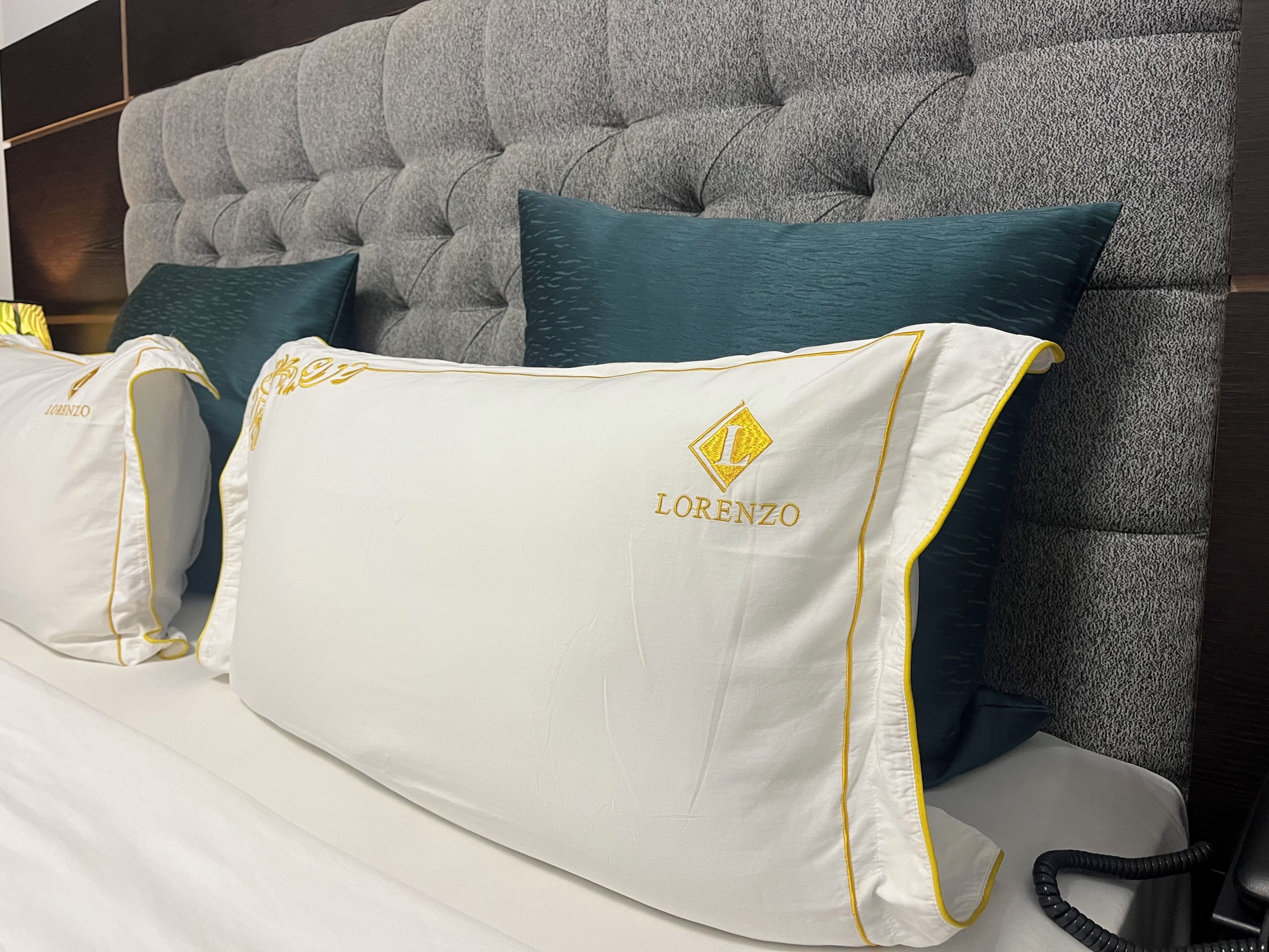 Cama com almofadas brancas e cabeceira cinza com textura estufada.