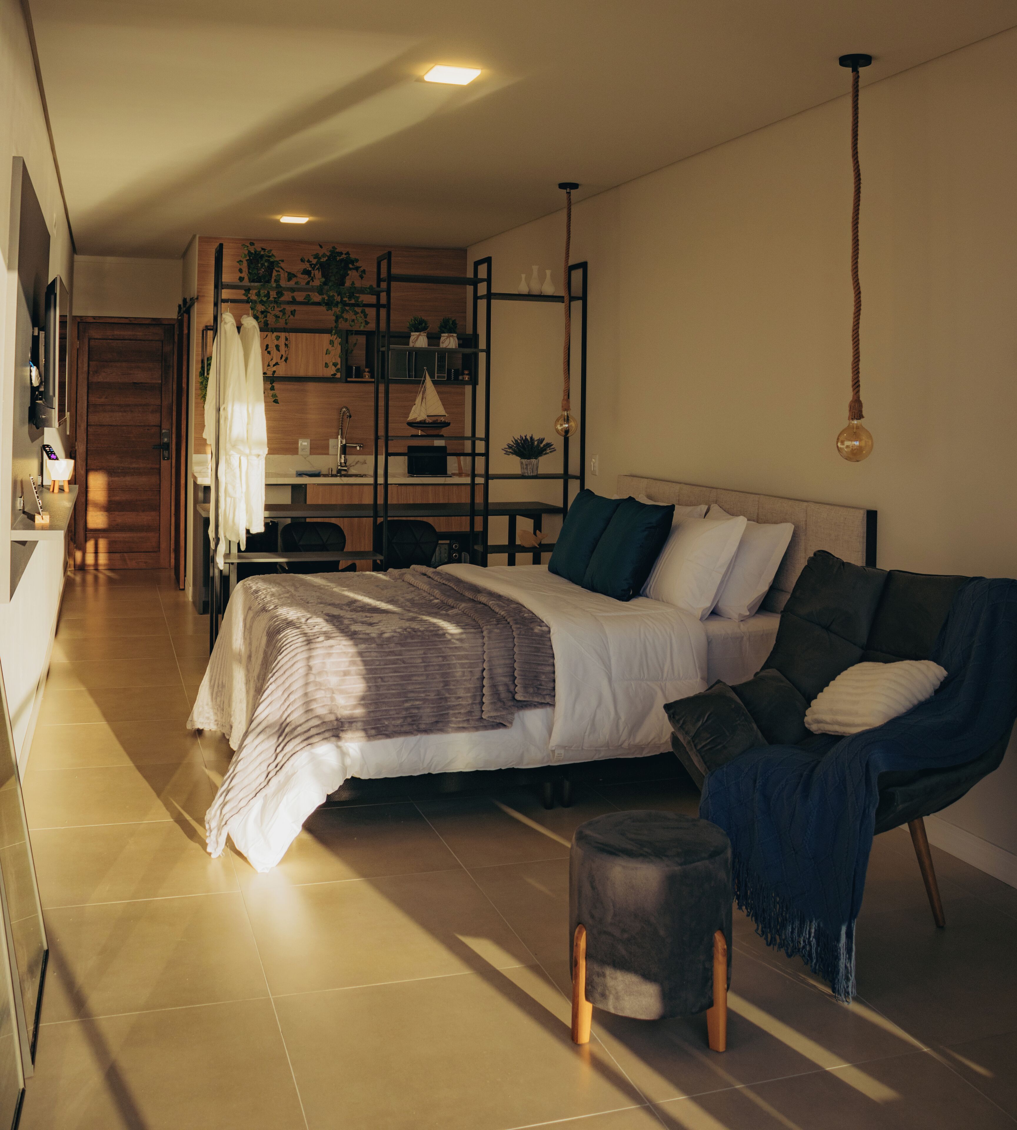 Quarto moderno com uma cama, um sofá, uma mesinha e um candeeiro suspenso.