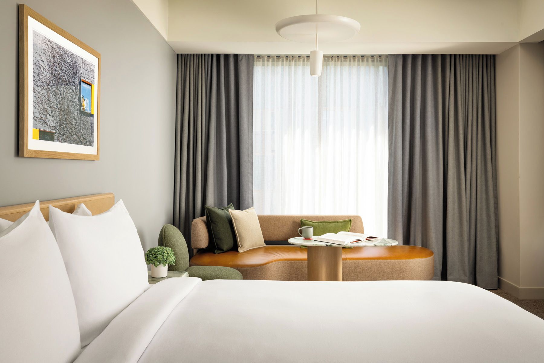 Quarto de hotel com uma cama grande, área de estar com mesa e janela com cortinas.