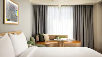 Quarto de hotel com uma cama grande, área de estar com mesa e janela com cortinas.